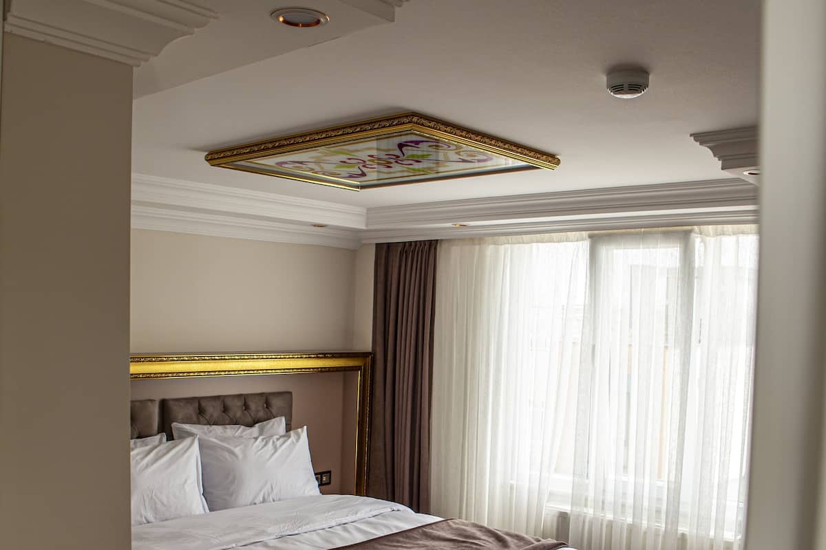 Quarto de hotel com uma cama grande, um banco e um lustre.