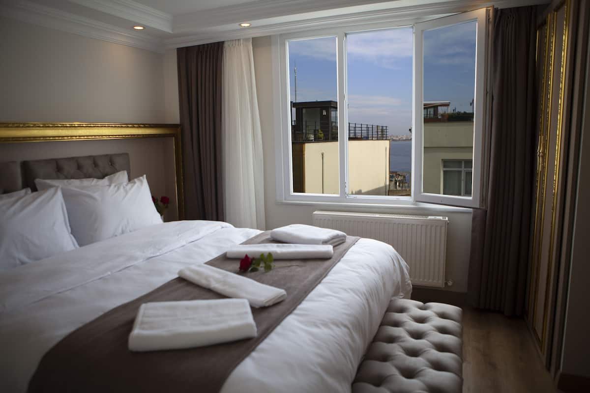 Quarto de hotel com uma cama grande, vista da cidade pela janela e uma varanda.