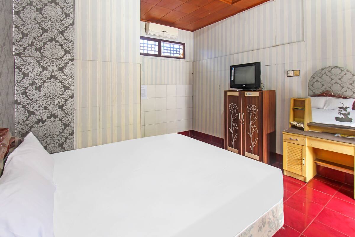 Quarto de hotel com uma cama, escrivaninha de madeira, televisão e guarda-roupa.