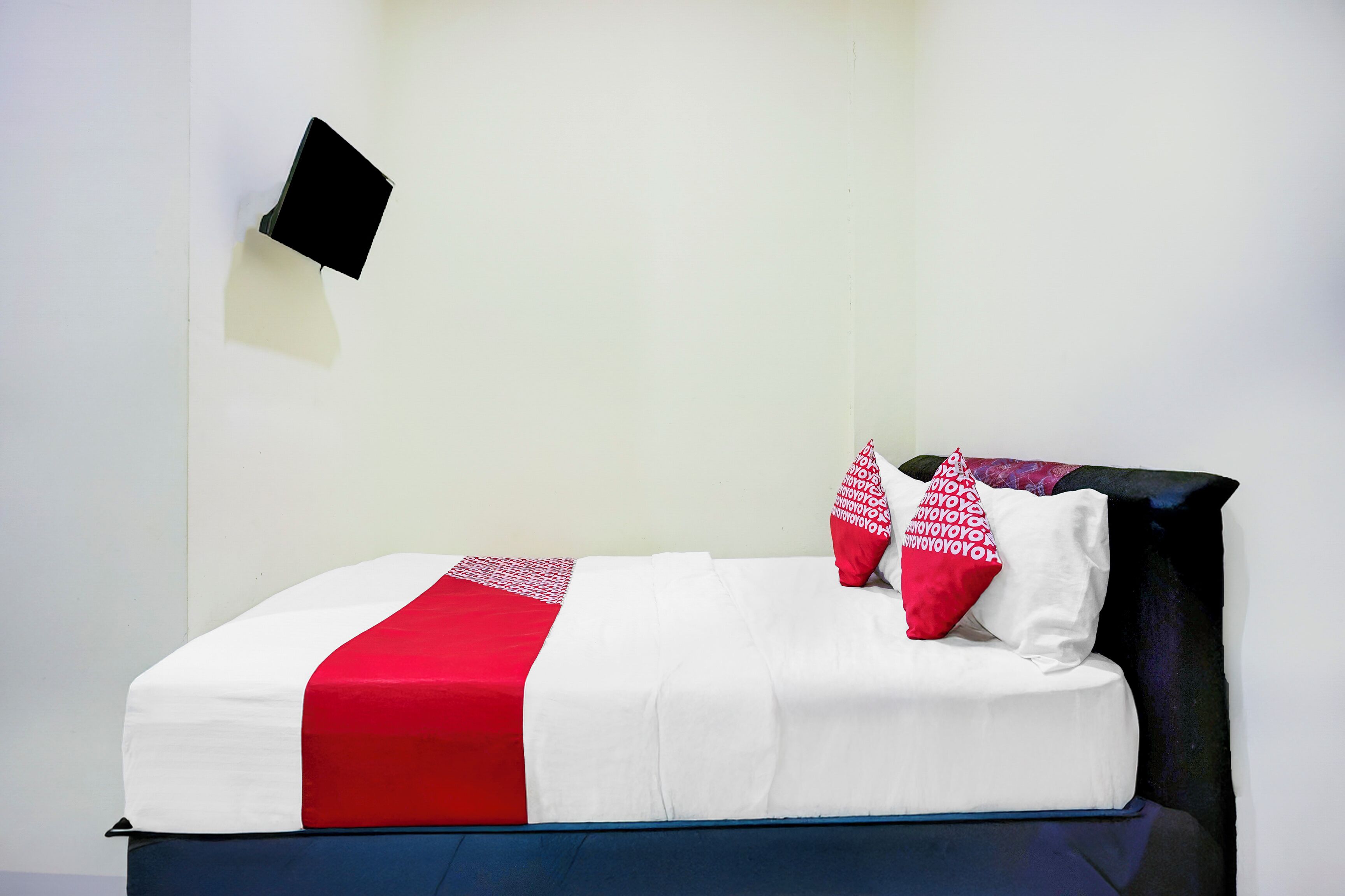Uma cama com colcha vermelha e branca, duas almofadas vermelhas e uma cabeceira preta.