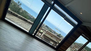 Quarto espaçoso com grandes janelas que oferecem vista para uma paisagem rochosa e o mar.