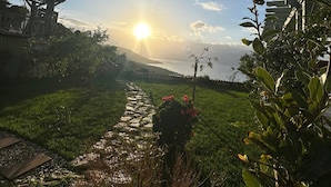 Caminho de jardim que leva a um gazebo com vista para o mar e o sol se pondo ao fundo.