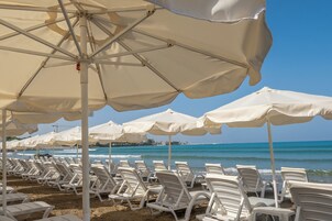 Uma praia com fileiras de cadeiras de praia brancas e grandes guarda-sóis brancos.