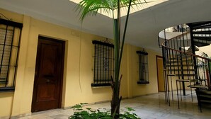 Um espaço amplo e interno com uma planta em vaso central, piso em ladrilho e uma escada em caracol.