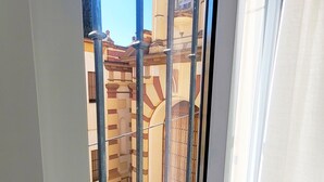 Visão através de uma janela com grades de um edifício com chão de azulejos e uma porta com portão de metal.