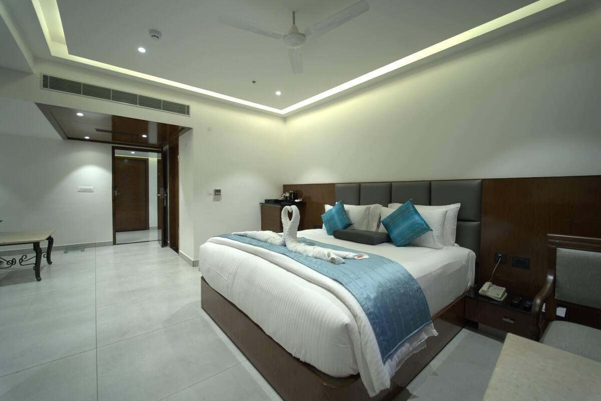 Quarto de hotel moderno com uma cama grande, mesas de cabeceira, escrivaninha e ventoinha no teto.