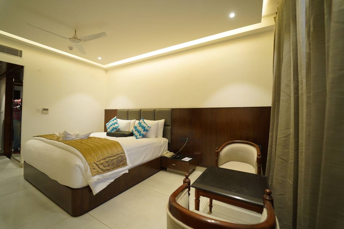 Quarto de hotel com cama, mesa de cabeceira, cadeira e ventilador de teto.