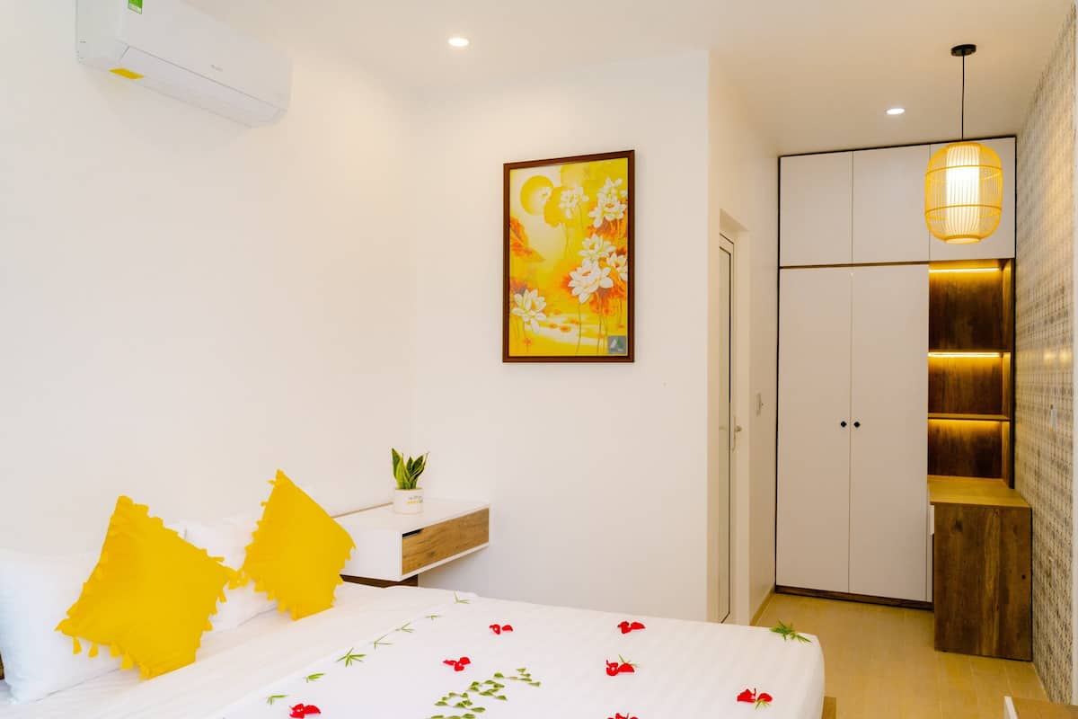 Quarto com cama, mesa de cabeceira com planta, guarda-roupa e luminária suspensa.