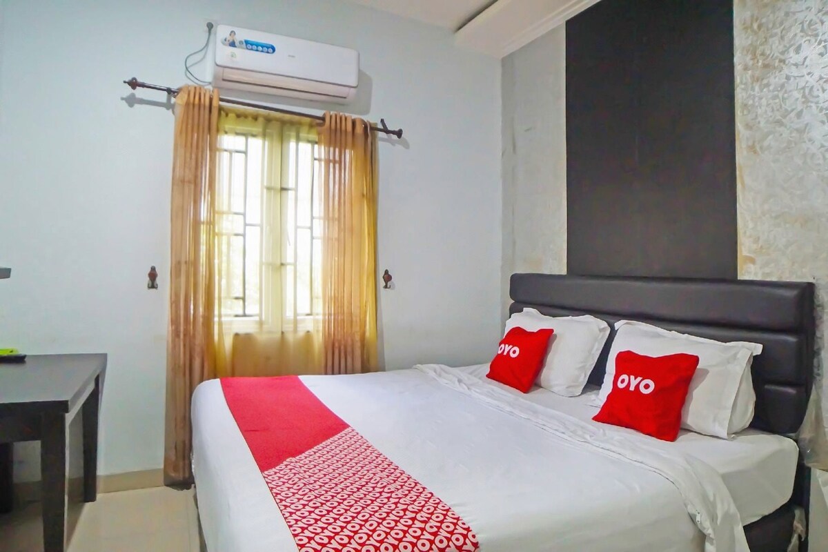 Quarto de hotel com cama, escrivaninha, ar condicionado e janela com cortinas.
