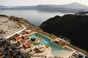 Piscina de resort com espreguiçadeiras e guarda-sóis, emoldurada por paisagem natural e com vista para um corpo d'água.