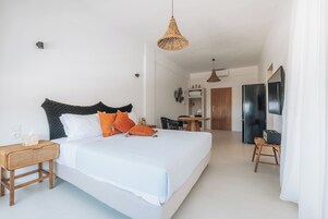 Quarto de hotel moderno com uma cama grande, uma mesa pequena, televisão e cozinha compacta.