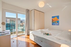 Quarto de hotel com cama, escrivaninha, cadeira, guarda-roupa e varanda com vista para a cidade.