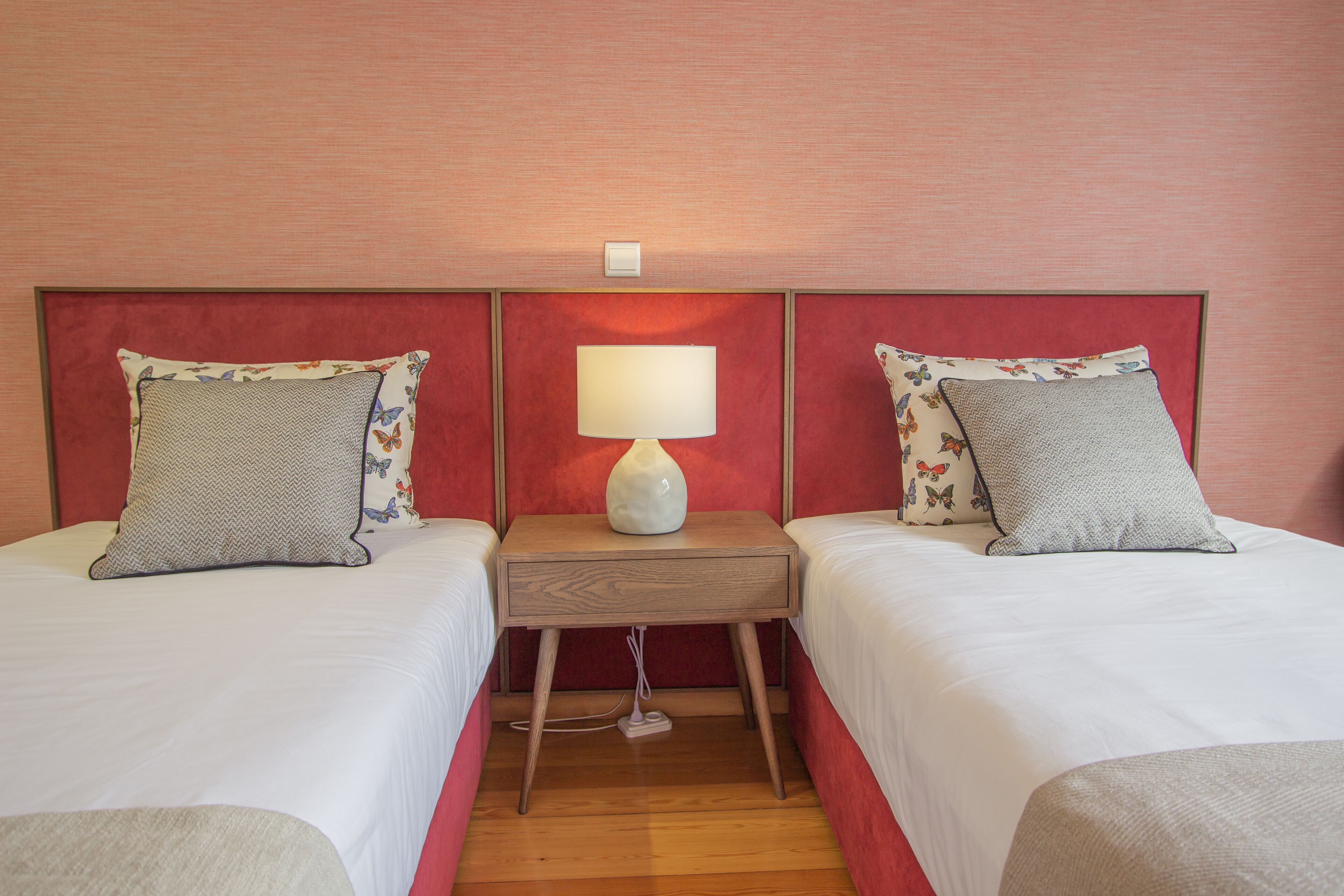 Quarto de hotel com duas camas, cada uma com almofada e mesa de cabeceira com abajur.