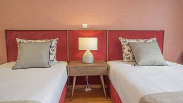 Quarto de hotel com duas camas, cada uma com almofada e mesa de cabeceira com abajur.