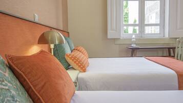 Quarto de hotel com duas camas, uma luminária, uma janela e uma pequena mesa.