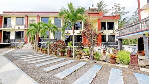 Um hotel com vários andares e um pátio central com palmeiras, plantas em vasos e um caminho de pedra.