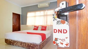 Quarto de hotel com cama, porta de madeira e um aviso com a inscrição 'DND'.