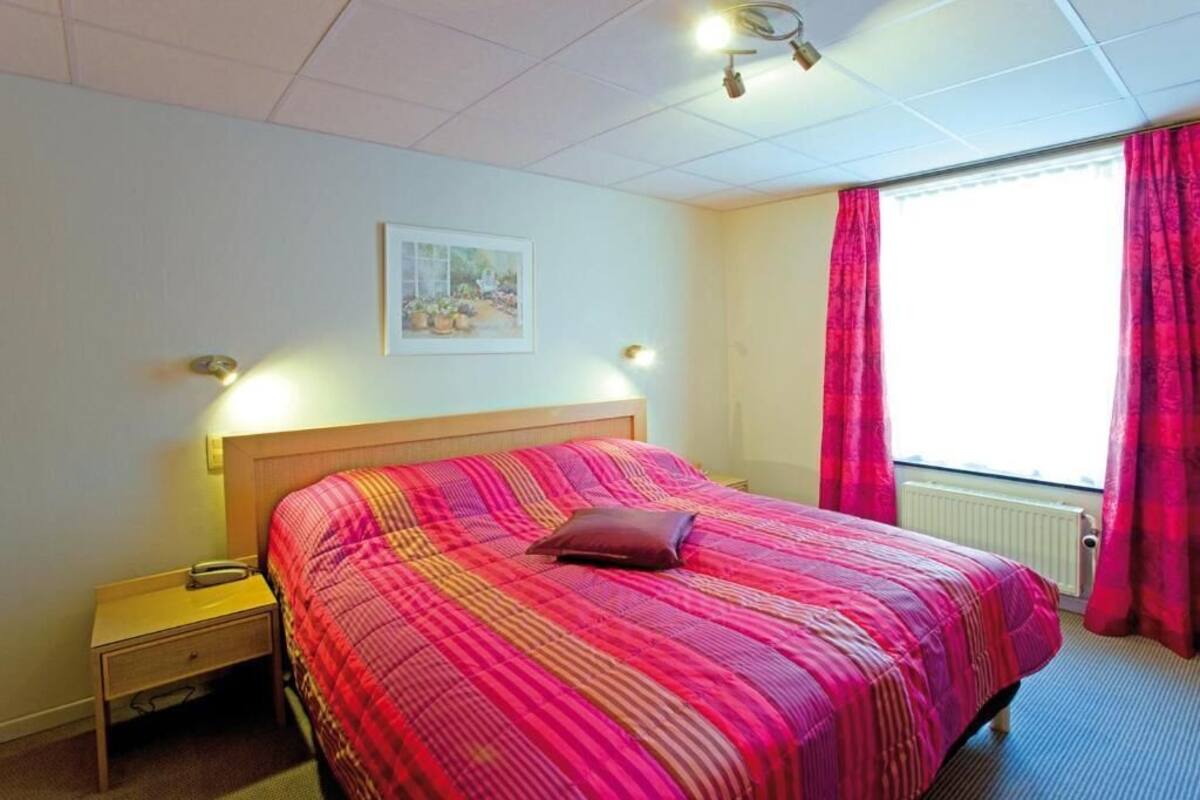 Quarto de hotel com cama, mesa de cabeceira, um quadro na parede e uma janela com cortinas.