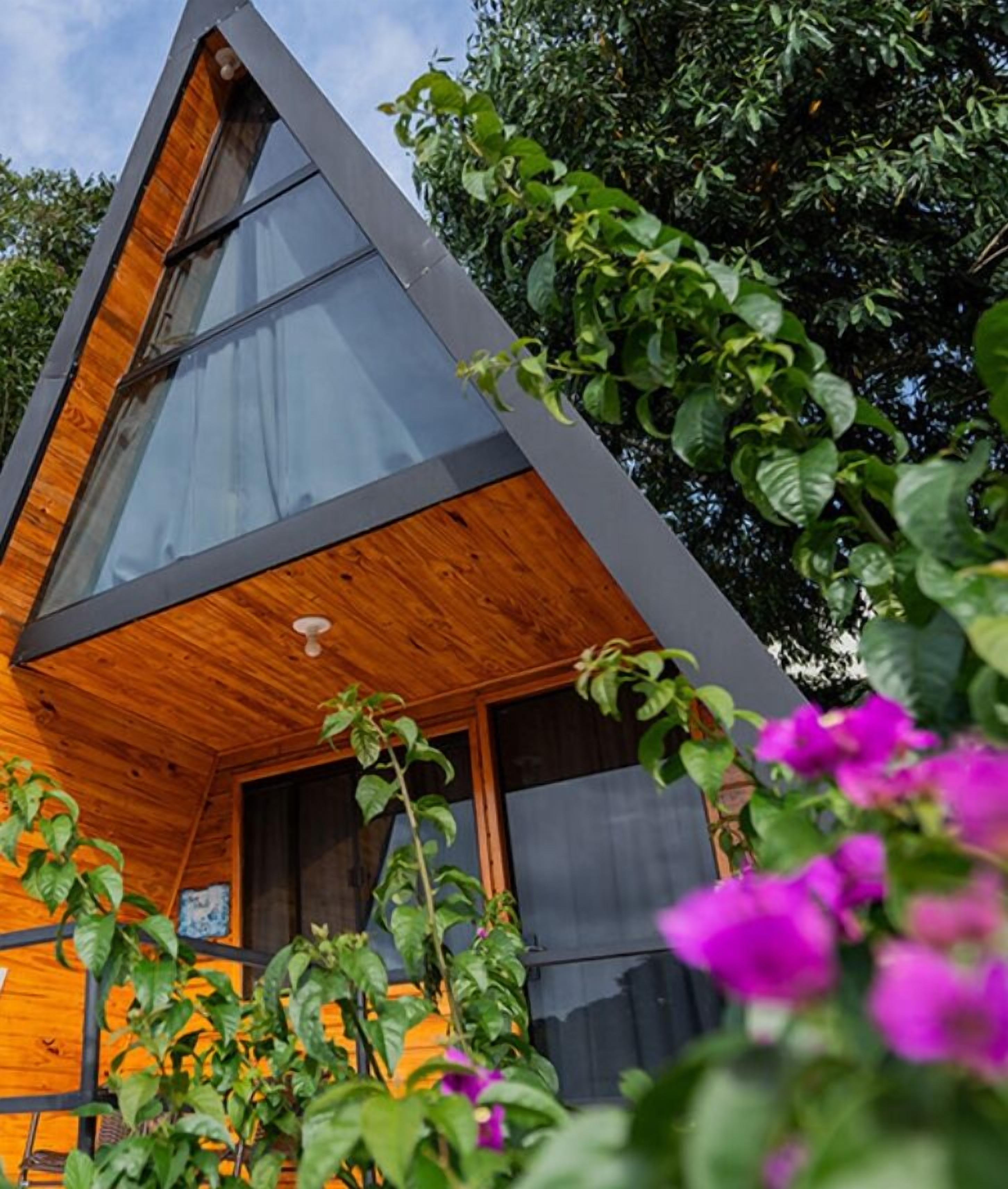 Uma cabana moderna de madeira, com design triangular, grandes janelas e teto de madeira.