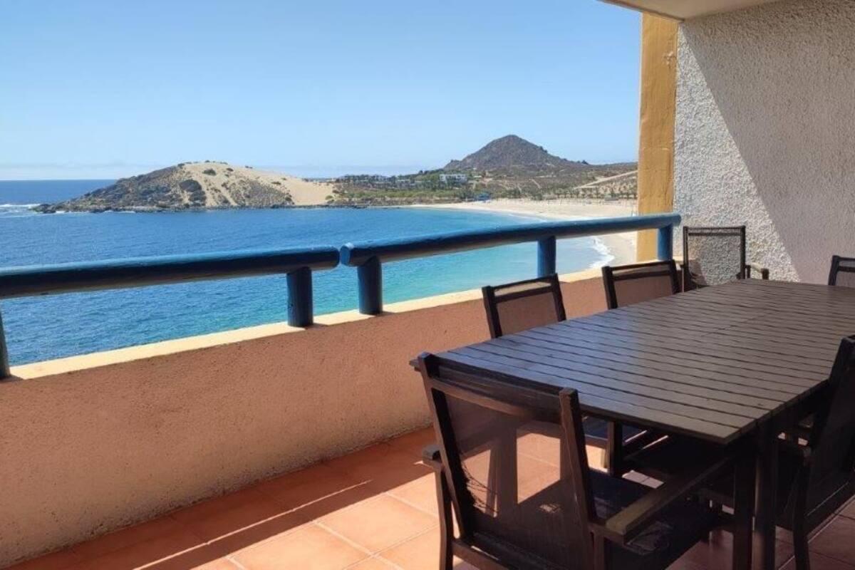 Varanda com mesa e cadeiras de frente para uma praia e oceano.