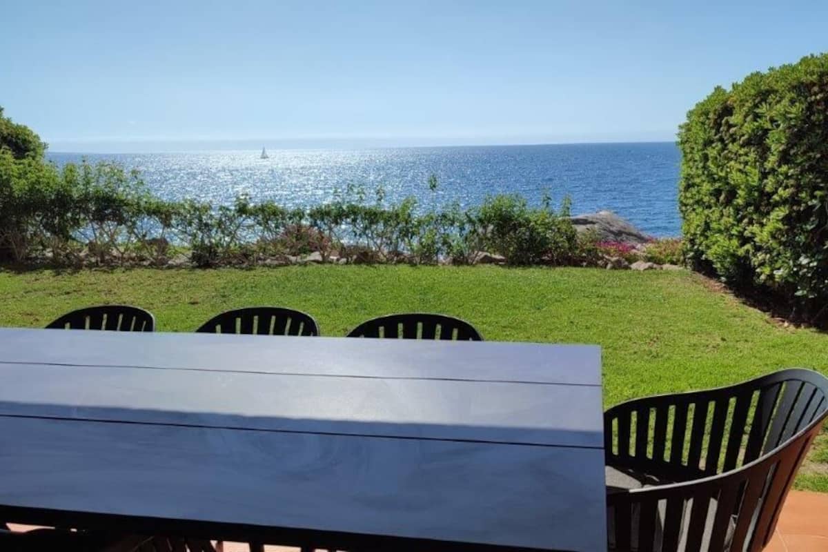 Um pátio com mesa e cadeiras, vista para o oceano e um jardim bem cuidado.
