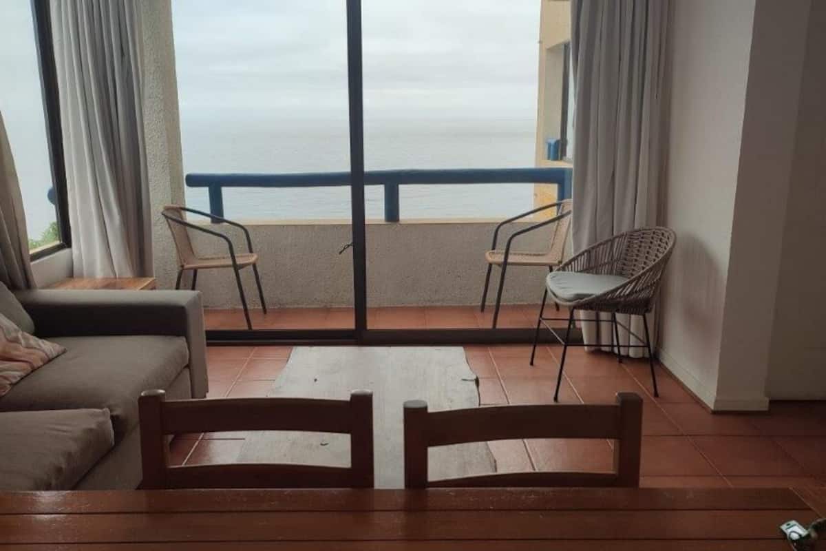 Uma varanda com vista para o mar, um sofá, duas cadeiras e uma mesa de madeira.
