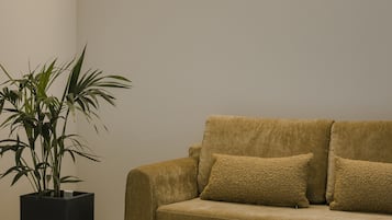 Uma sala de estar moderna com um sofá bege, duas mesinhas redondas e um vaso com planta.