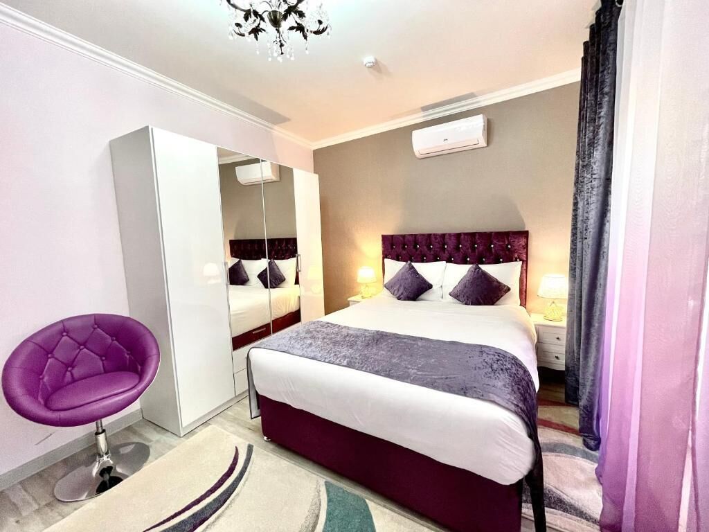 Quarto com cama, uma cadeira roxa, guarda-roupa e espelho.
