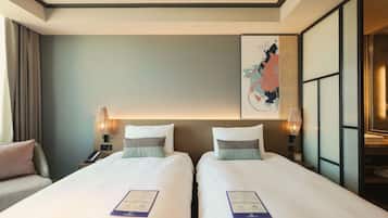 Quarto de hotel com duas camas, mesa de cabeceira com telefone, luminária e uma obra de arte na parede.