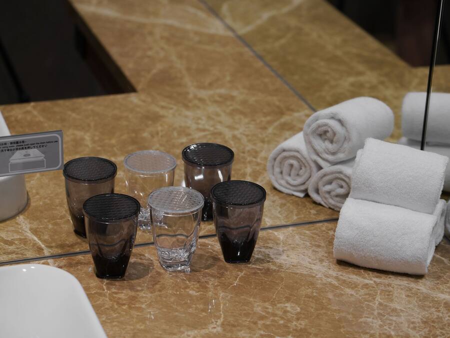 Uma mesa com tampo de mármore, copos pretos, um copo e toalhas brancas dobradas.