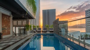 Piscina no terraço com vista para o horizonte urbano e um pôr do sol.