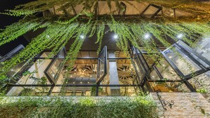 Um edifício moderno com vários andares, grandes janelas de vidro e trepadeiras verdes cobrindo as paredes externas.
