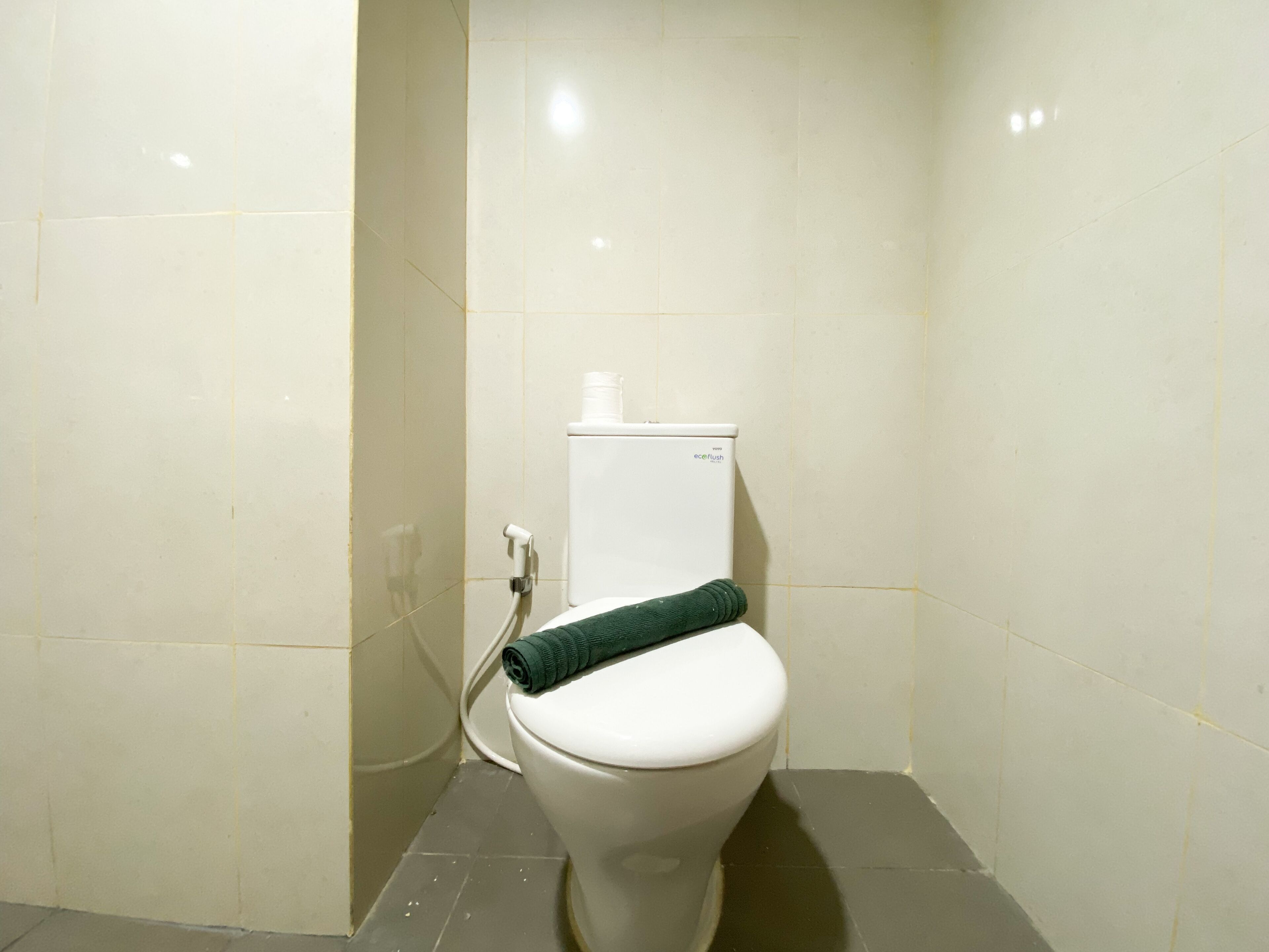 Casa de banho pequena e limpa, com sanita branca, toalha verde e suporte de papel higiénico branco.