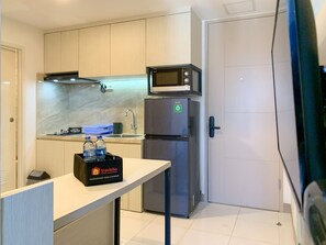 Uma cozinha compacta com micro-ondas, geladeira e um bebedouro no balcão.