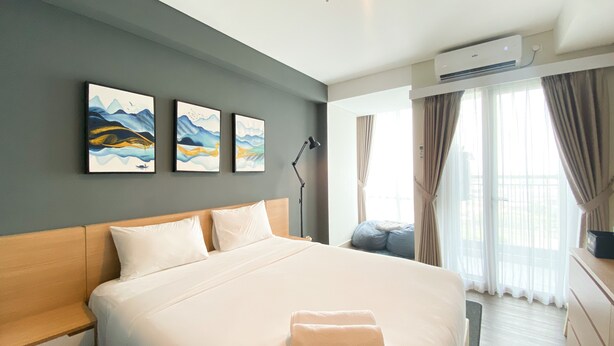 Quarto de hotel com uma cama grande, uma mesinha de cabeceira, uma luminária e três obras de arte emolduradas na parede.
