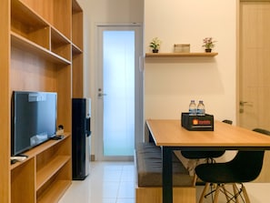 Quarto de hotel com suporte de TV de madeira, televisão de tela plana, bebedouro, mesa com bandeja de água engarrafada e porta que dá para o exterior.