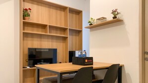 Um espaço compacto com mesa de jantar de madeira, duas cadeiras, televisão e estantes embutidas com plantas em vasos.