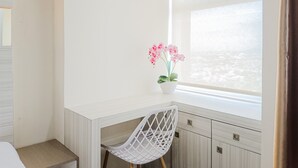 Mesa de canto com uma cadeira branca, planta em vaso com flores cor-de-rosa e janela com vista para uma paisagem nevada.