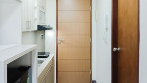 Quarto compacto com porta de madeira, micro-ondas e pequena área de cozinha.