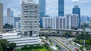 Um horizonte urbano moderno com um edifício branco de vários níveis em primeiro plano, rodeado por arranha-céus comerciais e uma autoestrada movimentada.