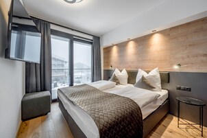Quarto de hotel moderno com uma cama grande, um espaço de estar pequeno, uma televisão e vista para a cidade.