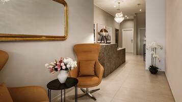 Um hall moderno com balcão de recepção, área de estar com uma cadeira e uma mesa pequena, e um vaso com flores.