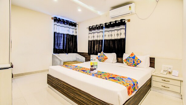 Quarto de hotel com uma cama grande, uma mesa de cabeceira, ar condicionado e uma janela com cortinas.