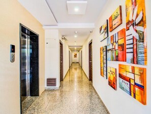 Corredor de hotel com piso de mármore, um elevador e arte abstrata colorida nas paredes.