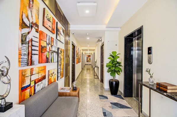 Corredor de hotel com sofá, obras de arte, planta em vaso e elevador.