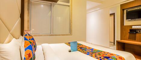 Quarto de hotel com cama, almofadas, manta colorida, televisão e janela.