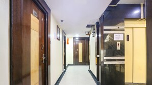 Corredor de hotel com portas de madeira e vidro, quartos numerados e um elevador com placa indicando uso exclusivo para pessoas.