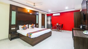Quarto de hotel com uma cama grande, uma escrivaninha com chaleira e uma parede de destaque vermelha.