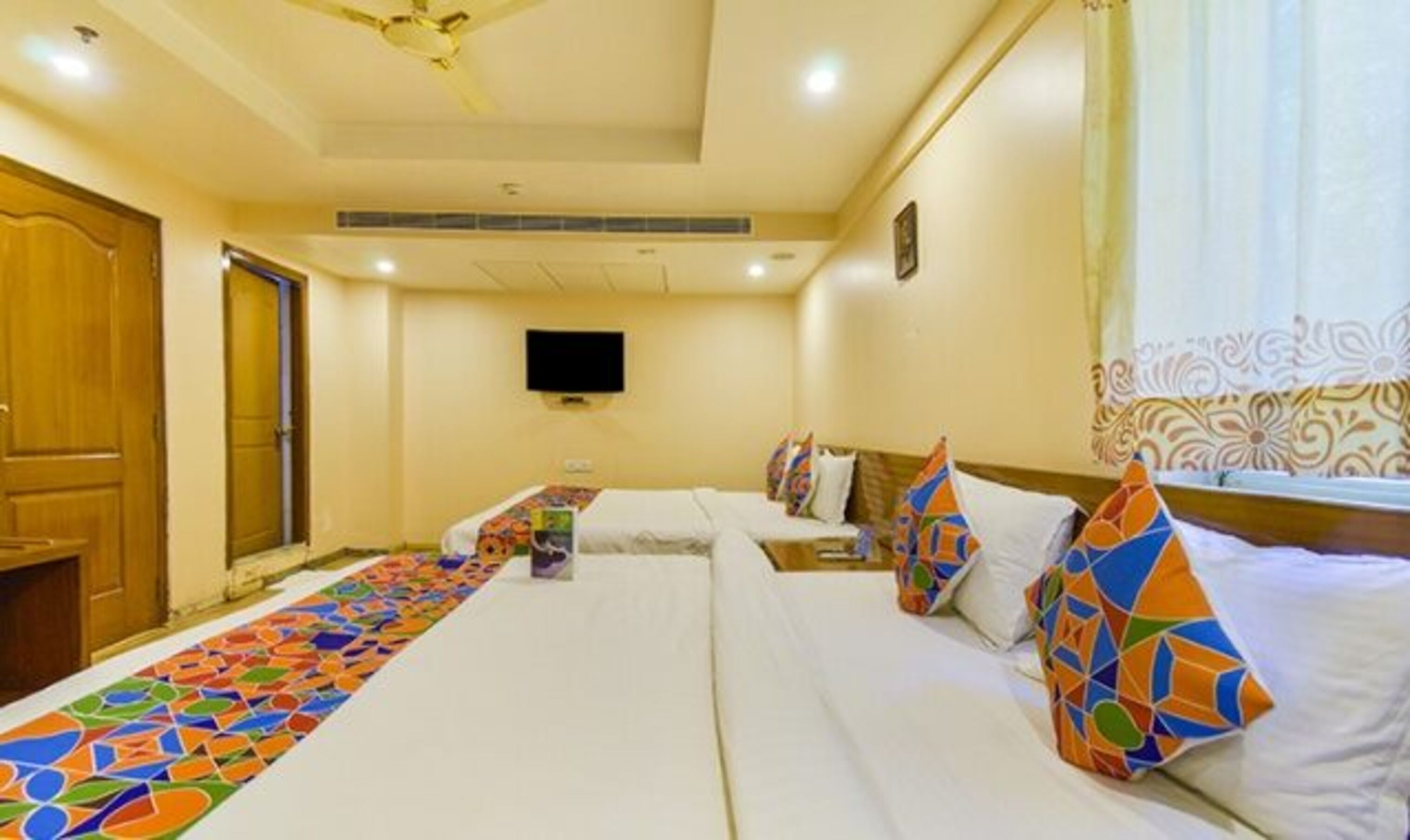 Quarto de hotel com duas camas, uma televisão na parede e um travesseiro decorativo.