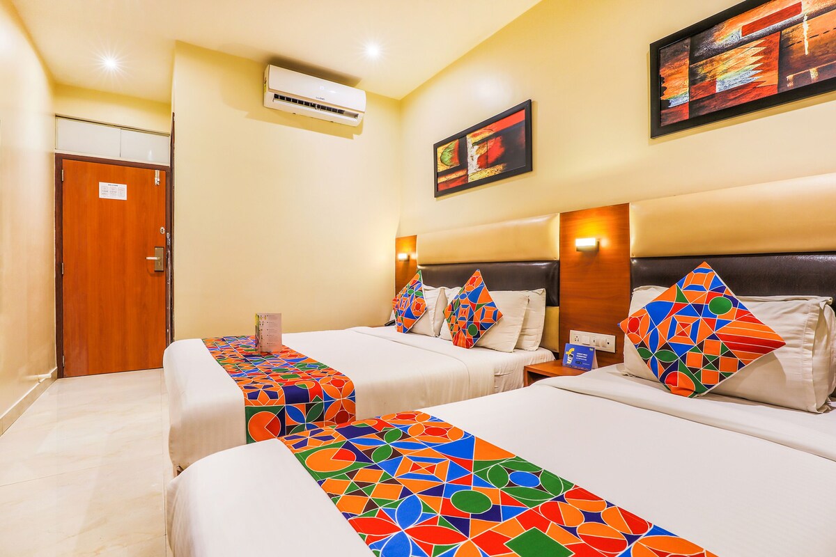 Quarto de hotel com duas camas, porta de madeira, aparelho de ar condicionado e um quadro na parede.